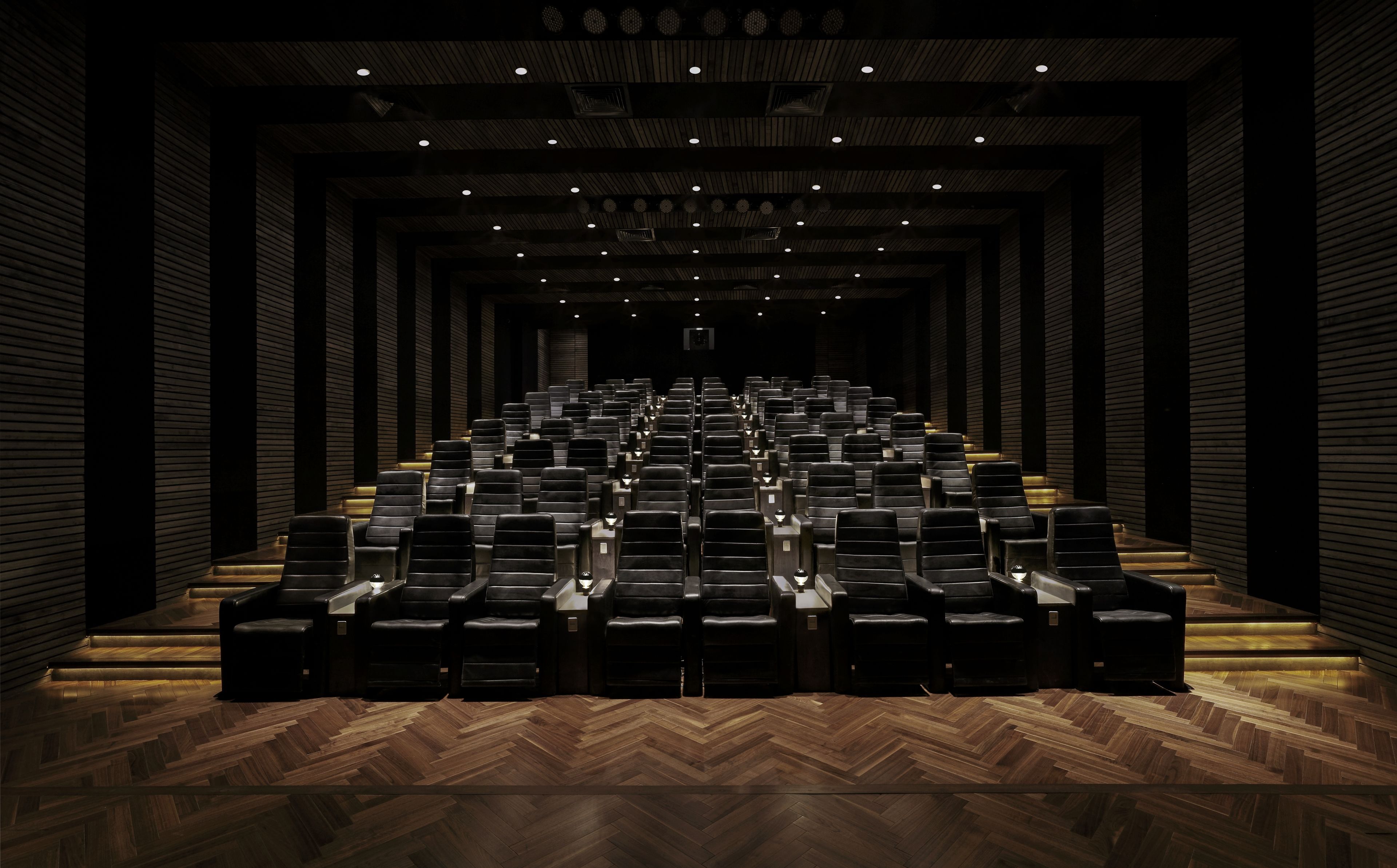 Um cinema com fileiras de assentos pretos e piso de madeira.