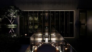 Uma entrada de edifício moderna com um espelho d'água refletivo e uma escadaria que leva ao interior.