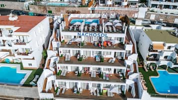 Um hotel com vários andares, área de piscina no terraço, várias varandas e uma placa com a inscrição "NACHOSOL".