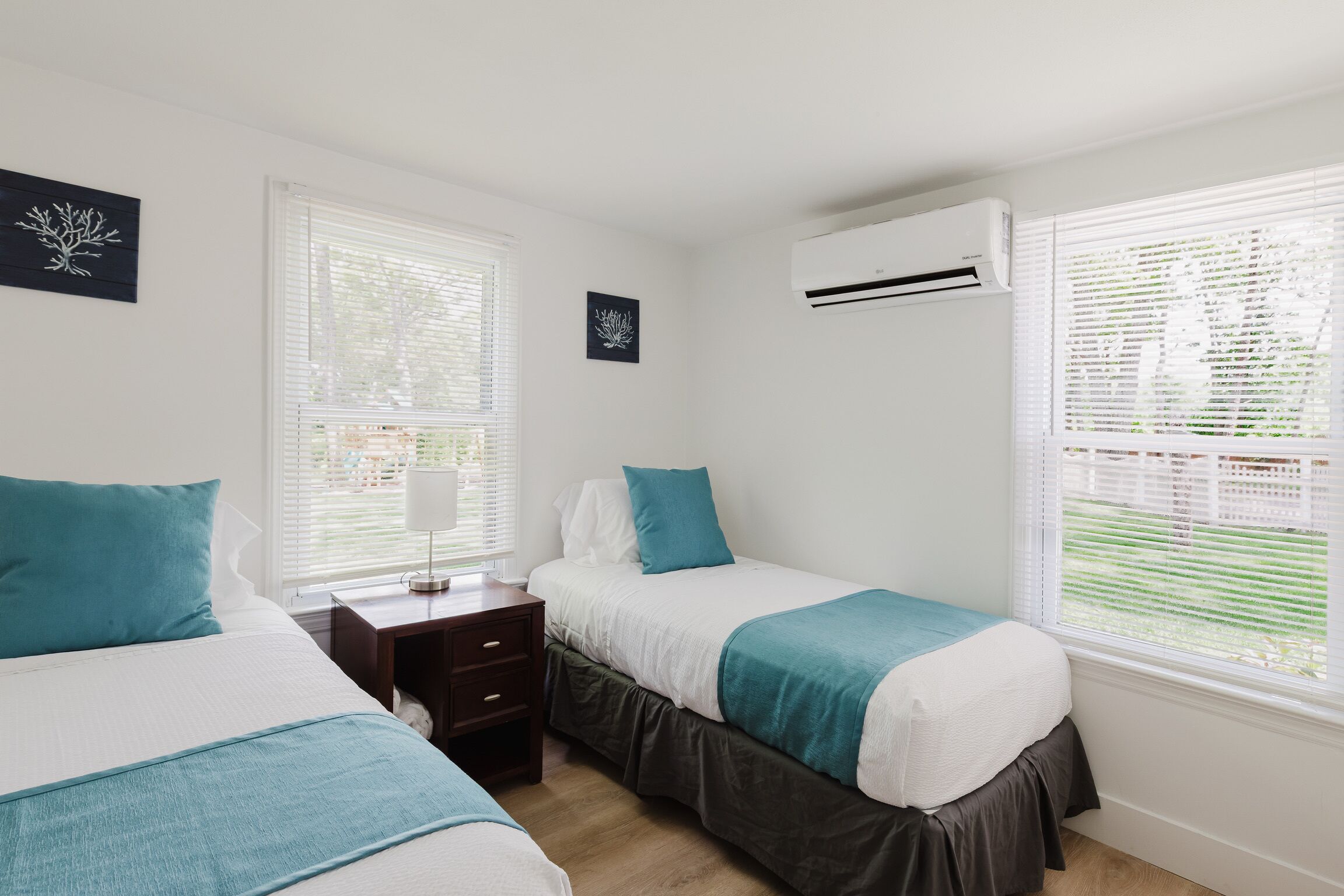 Quarto com duas camas, mesa de cabeceira, abajur e aparelho de ar condicionado.