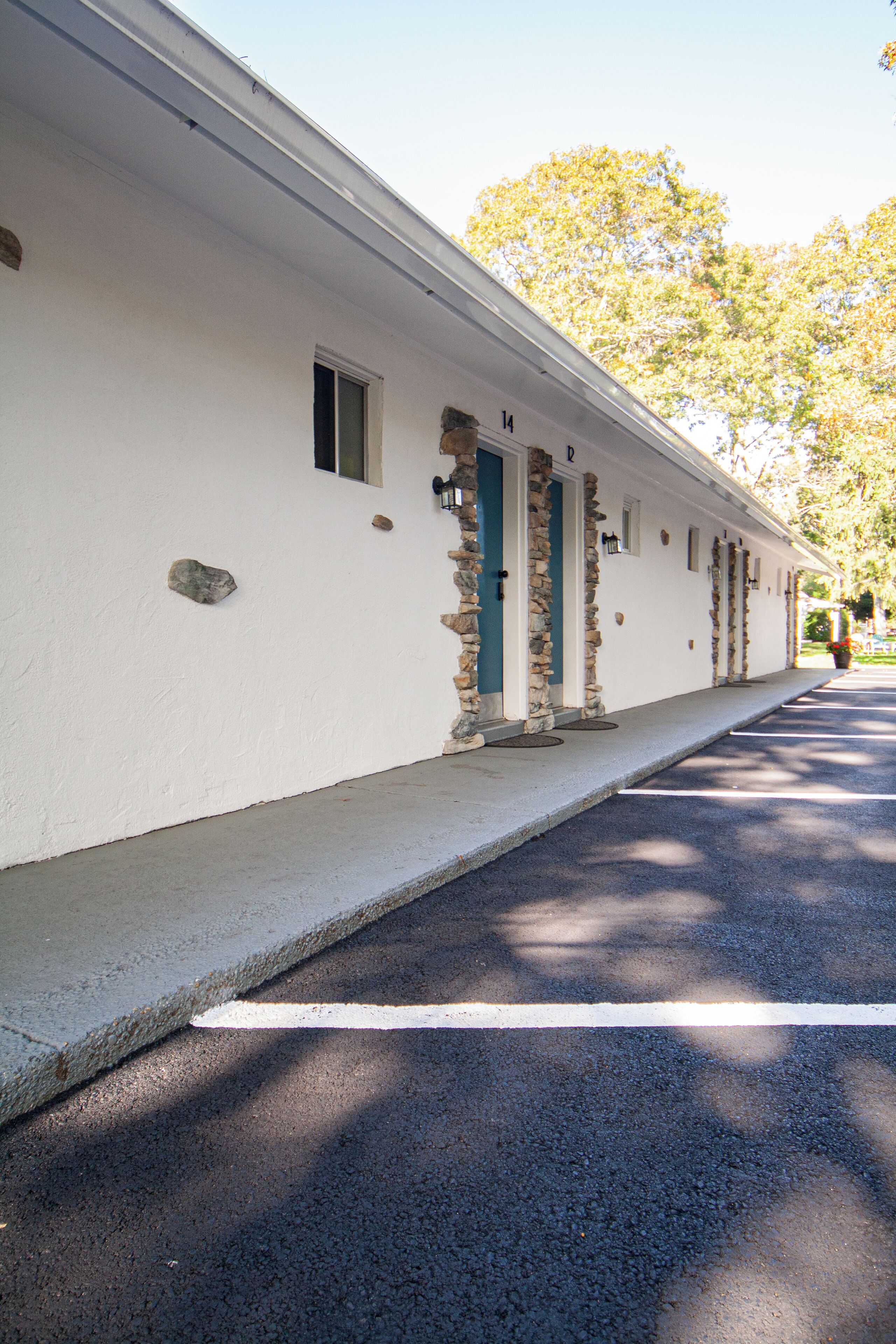 Fileira de quartos de motel com pilares de pedra, porta azul e fachada branca.