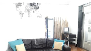 Quarto com sofá de couro preto e almofadas azuis e brancas, piso de madeira em padrão herringbone, e parede com design de mapa-múndi.