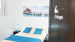 Quarto com uma cama, uma mesa de cabeceira, um abajur e uma parede com três quadros mostrando uma cena de praia.