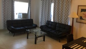 Uma sala de estar com dois sofás pretos, uma mesa de centro de vidro e uma luminária.