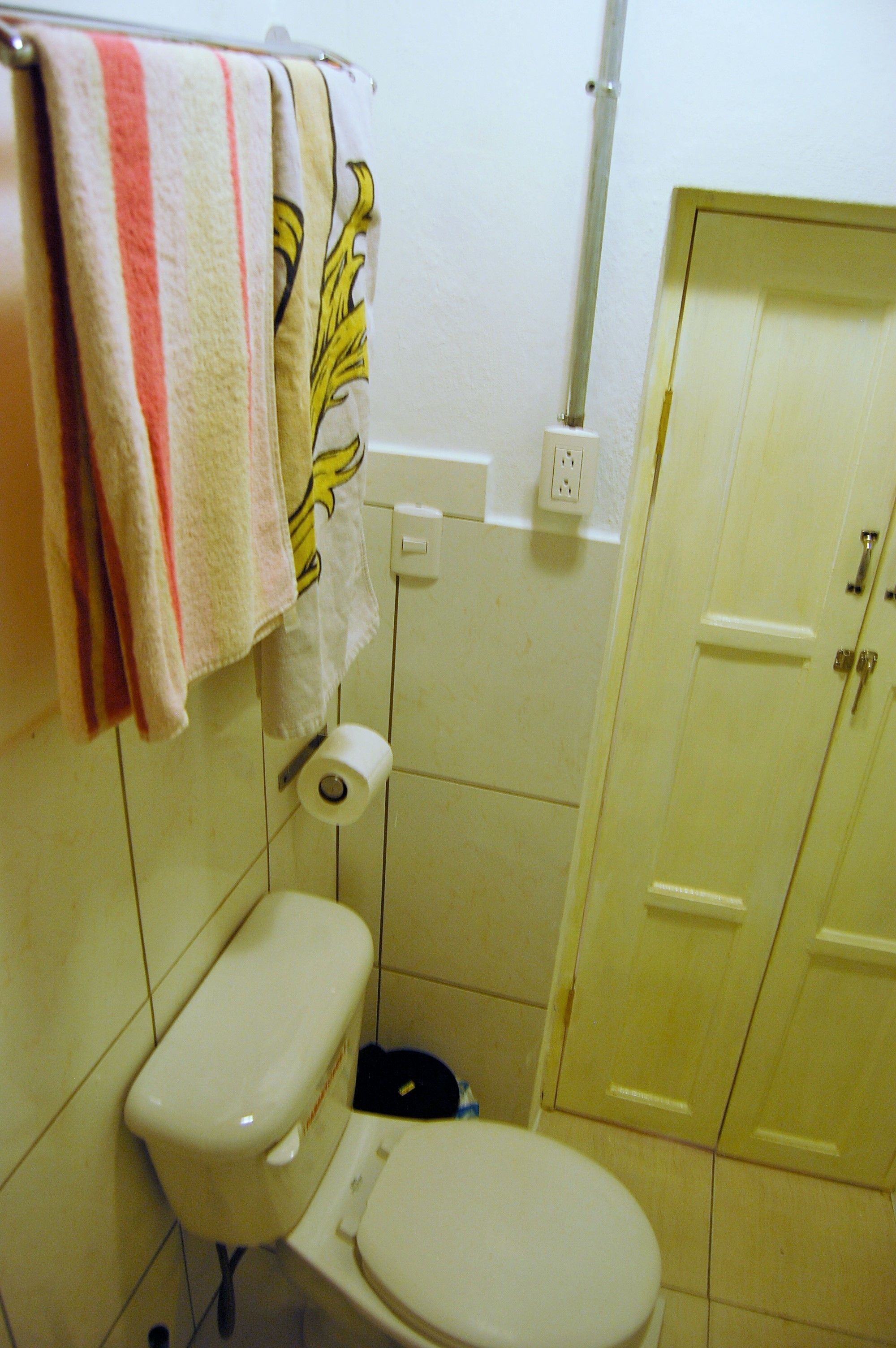Uma casa de banho pequena com sanita, um porta-toalhas com toalhas listradas, um rolo de papel higiénico e uma porta.