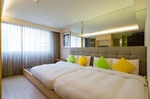 Quarto de hotel com uma cama grande, uma mesinha de cabeceira, um espelho e uma janela com cortinas.