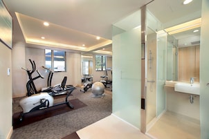 Quarto de hotel moderno com área de ginásio, incluindo equipamento de exercício e um espelho grande.