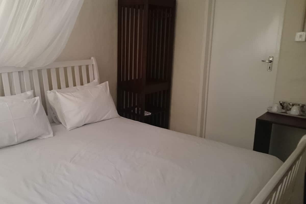 Uma cama bem arrumada com lençóis e almofadas brancos, cabeceira de madeira e um dossel.
