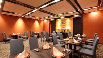 Sala de conferências com mesas montadas para uma reunião, equipada com cadeiras e tela de projeção.