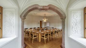Uma sala de conferências com uma mesa redonda, cadeiras de madeira e um lustre.
