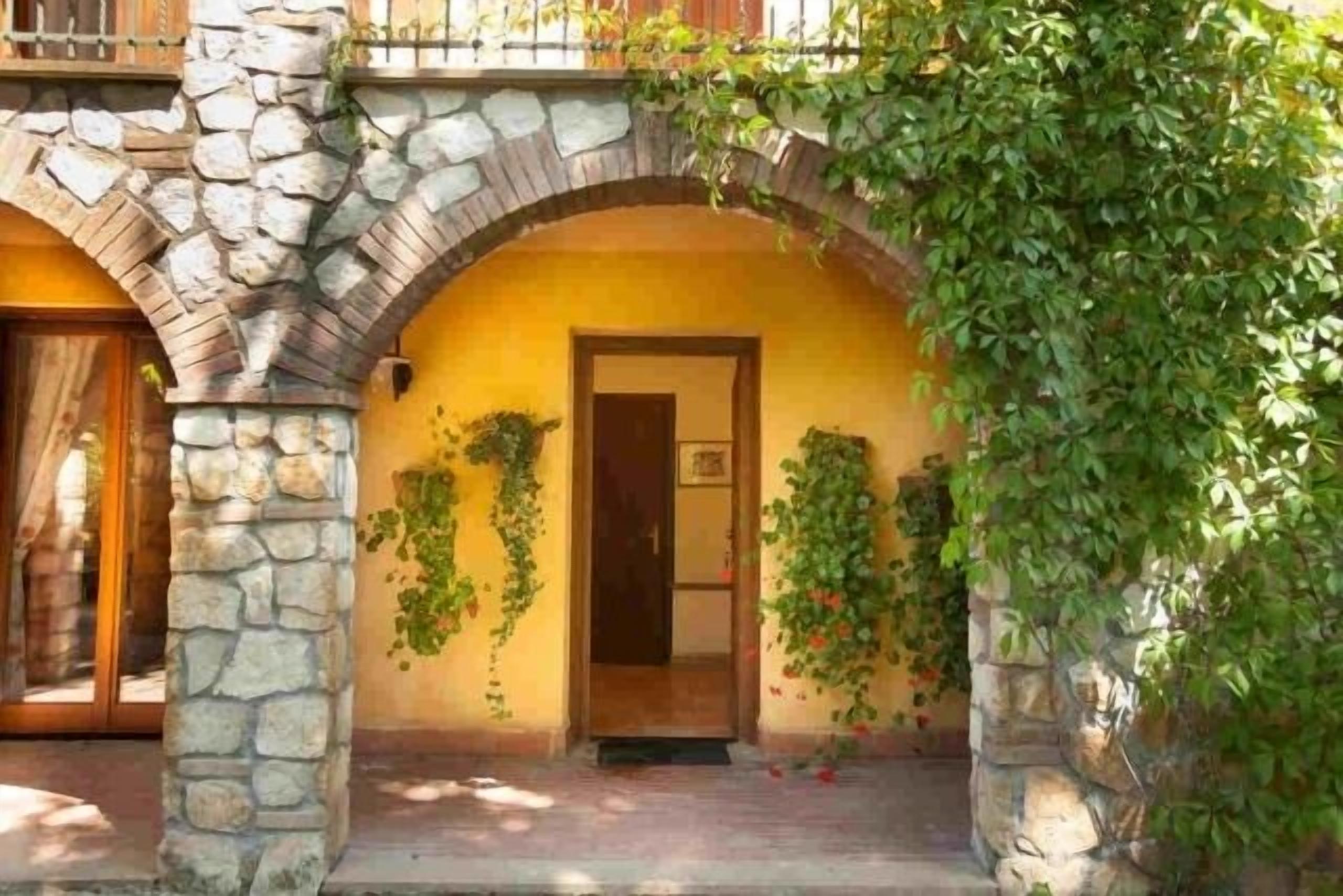 Arcada de pedra que dá para uma porta amarela, com uma varanda acima.