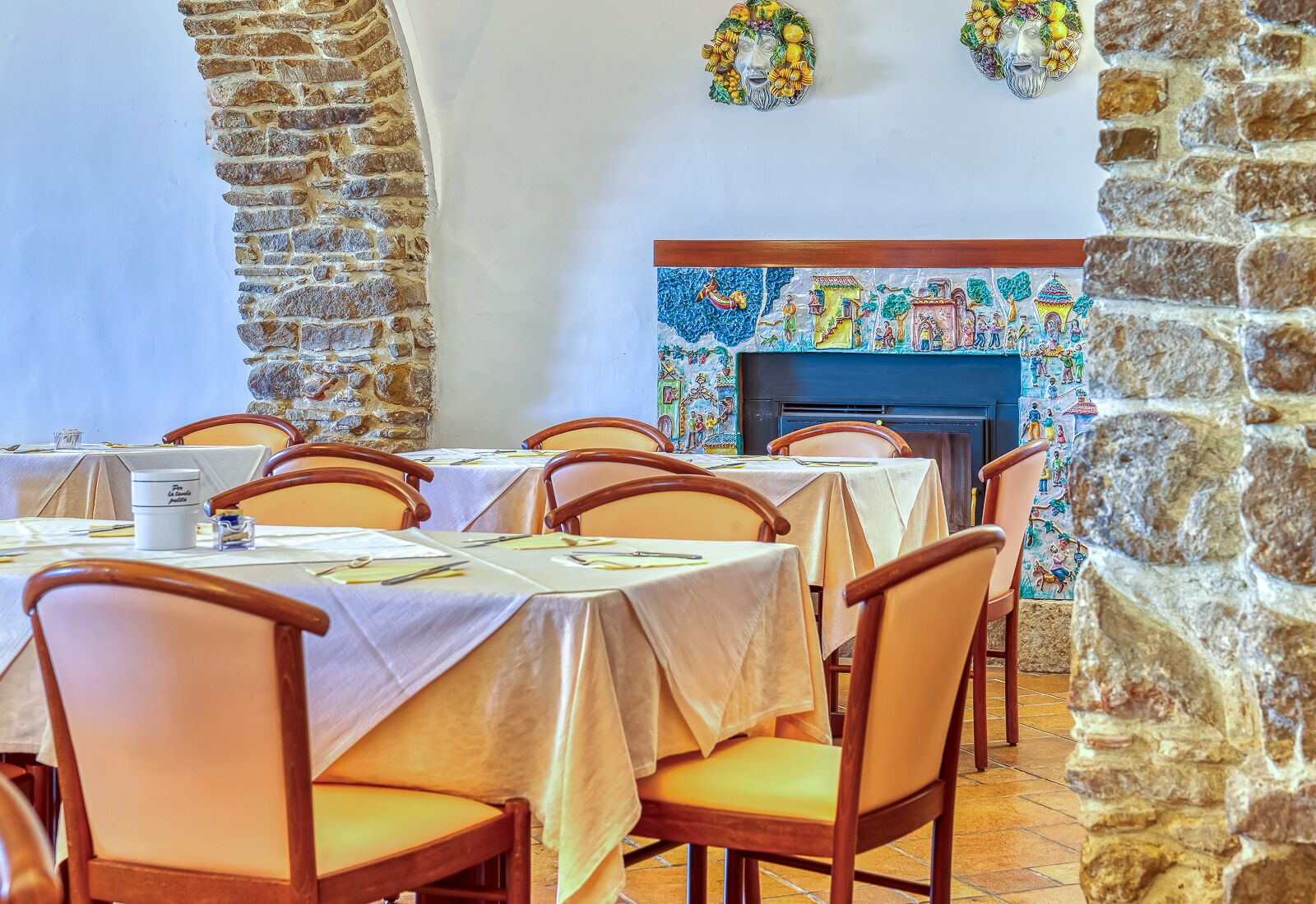 Uma sala de jantar com paredes de pedra, lareira em azulejos e cadeiras de madeira.
