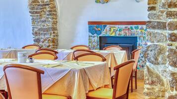 Uma sala de jantar com paredes de pedra, lareira em azulejos e cadeiras de madeira.
