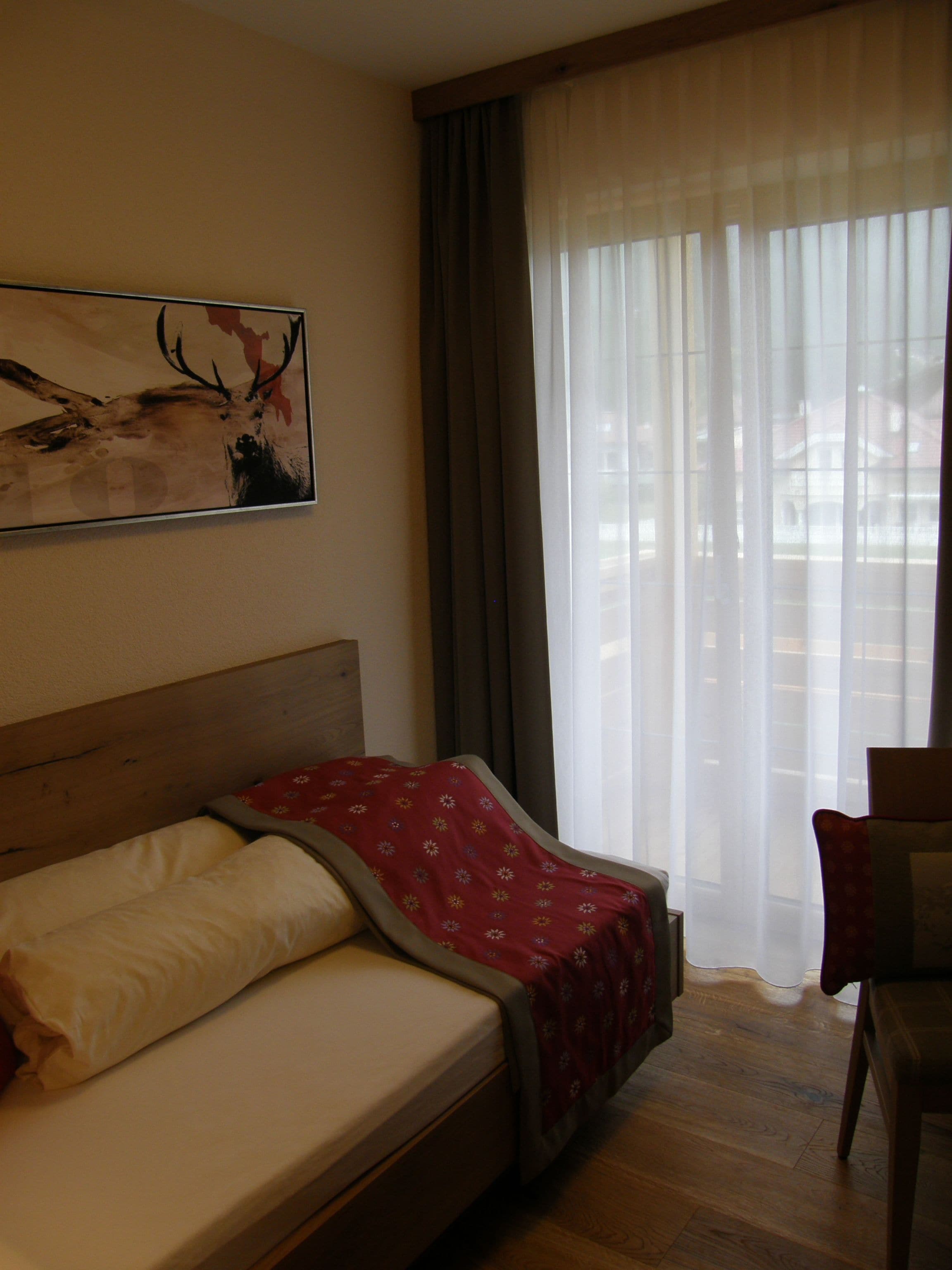 Quarto de hotel com cama, poltrona, quadro na parede e janela com cortinas.