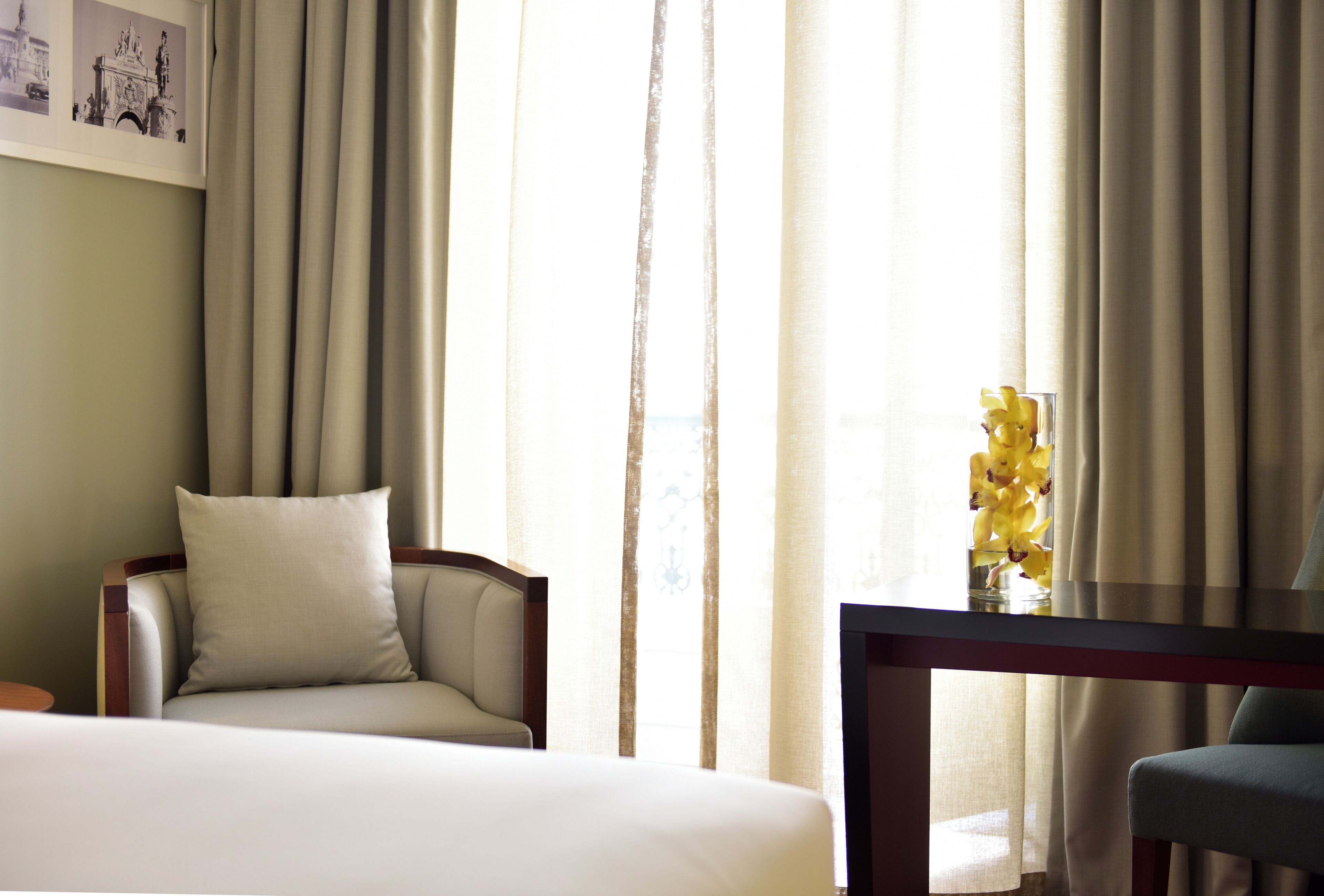 Quarto de hotel com cama, poltrona, mesa e janela com cortinas.