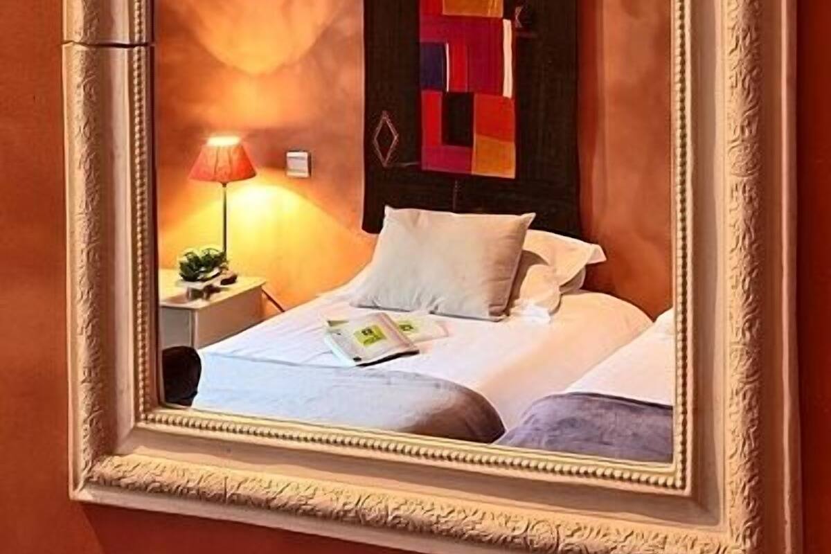 Quarto de hotel com cama, mesa de cabeceira, abajur e parede com padrão geométrico.