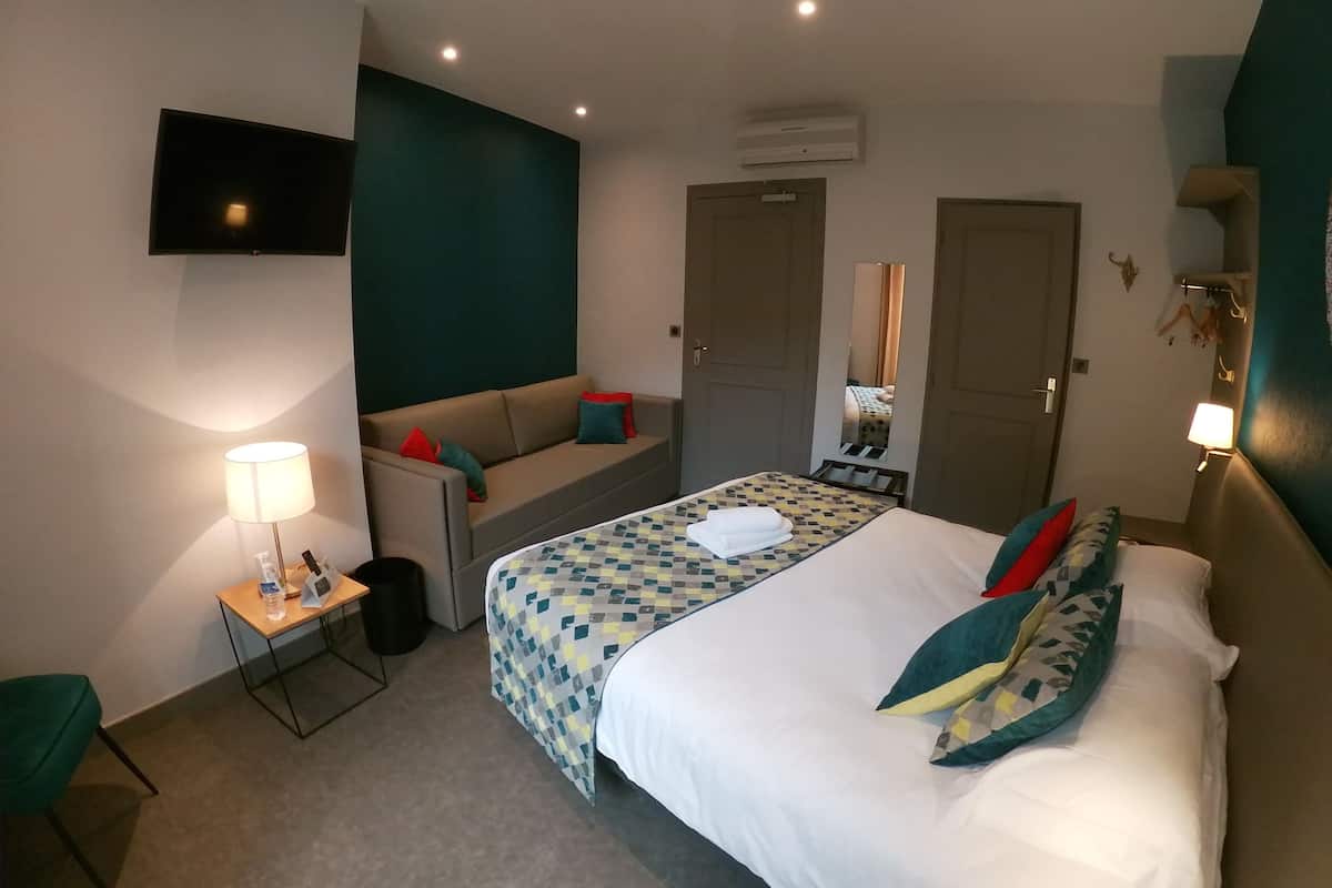 Quarto de hotel com cama, sofá, televisão, escrivaninha e espelho.