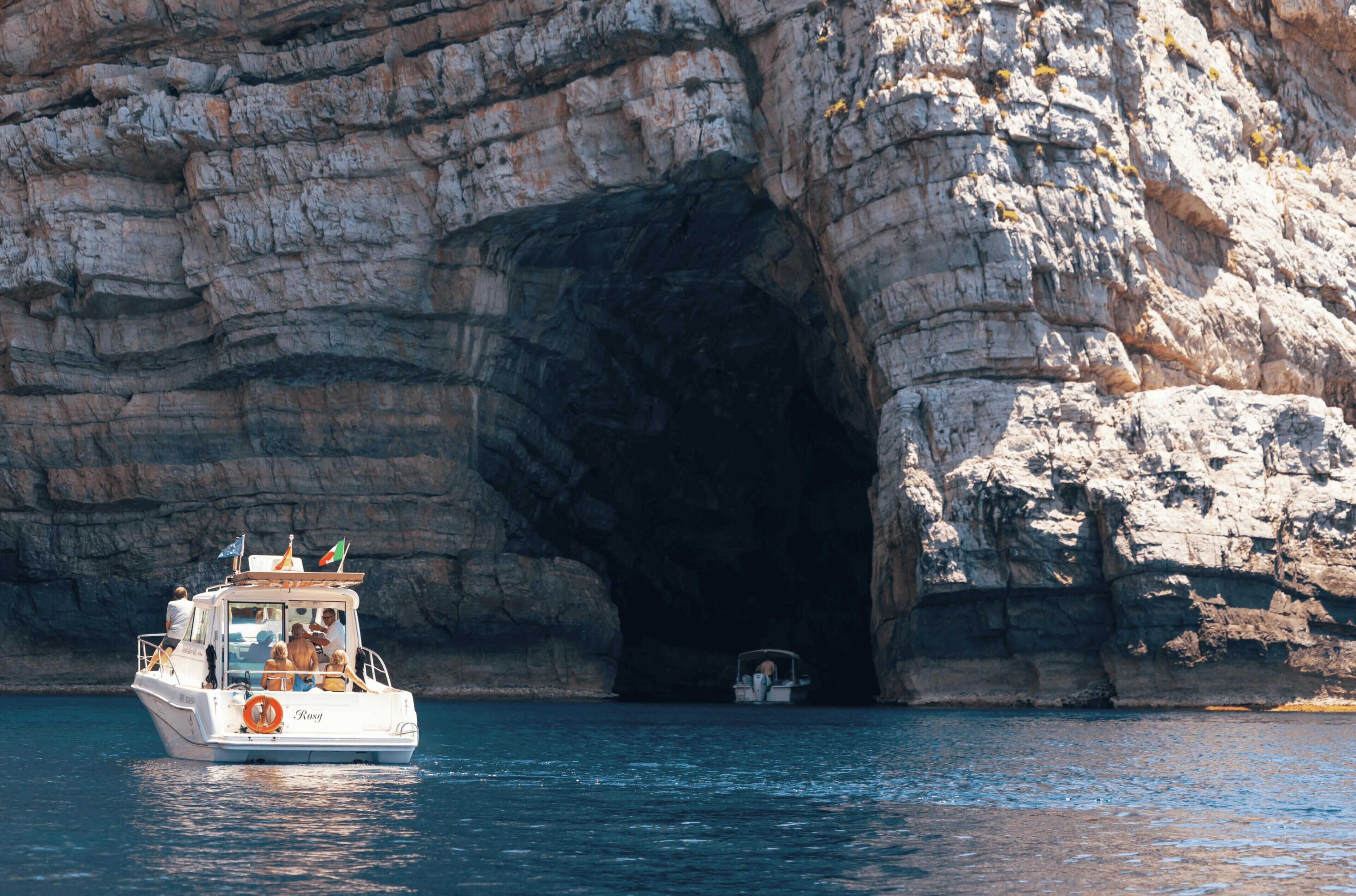Um barco chamado 'Rosy' atracado em uma área costeira rochosa, com uma grande formação semelhante a uma caverna ao fundo.