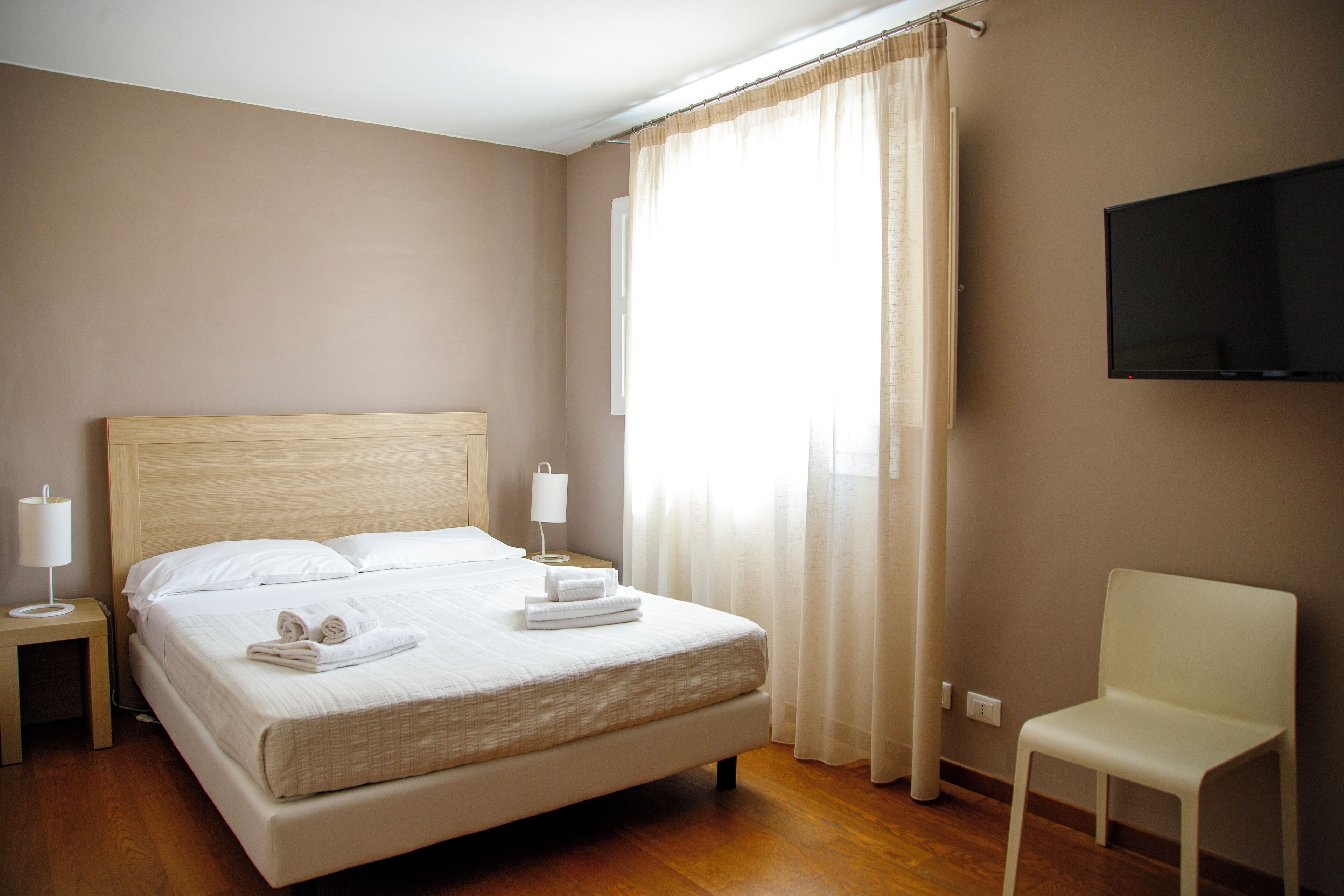 Quarto de hotel com cama grande, abajures, televisão e uma cadeira.