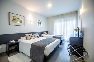 Quarto de hotel com duas camas, uma escrivaninha, uma cadeira, televisão e obras de arte nas paredes.