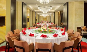 Uma sala de jantar de hotel com mesas redondas, cadeiras e um arranjo floral central.
