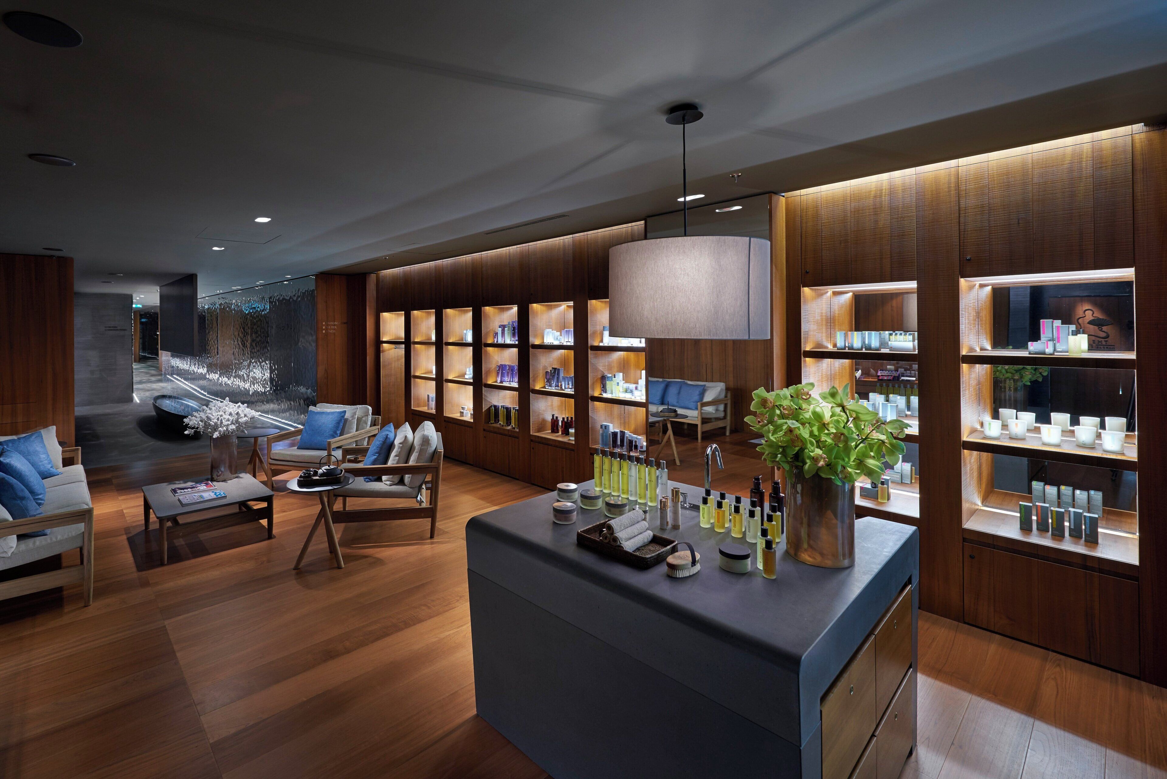 Um hall moderno de hotel com painéis de madeira, balcão de recepção, área de estar e prateleiras com amenities.