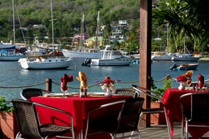 Uma área de refeições com mesas preparadas para dois, com vista para uma marina e barcos.