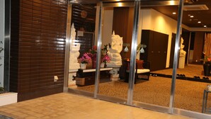 Entrada de um hotel com piso de azulejos, balcão de recepção e uma estátua de uma figura.