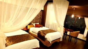 Quarto de hotel com duas camas, área de refeições e vista da cidade à noite.