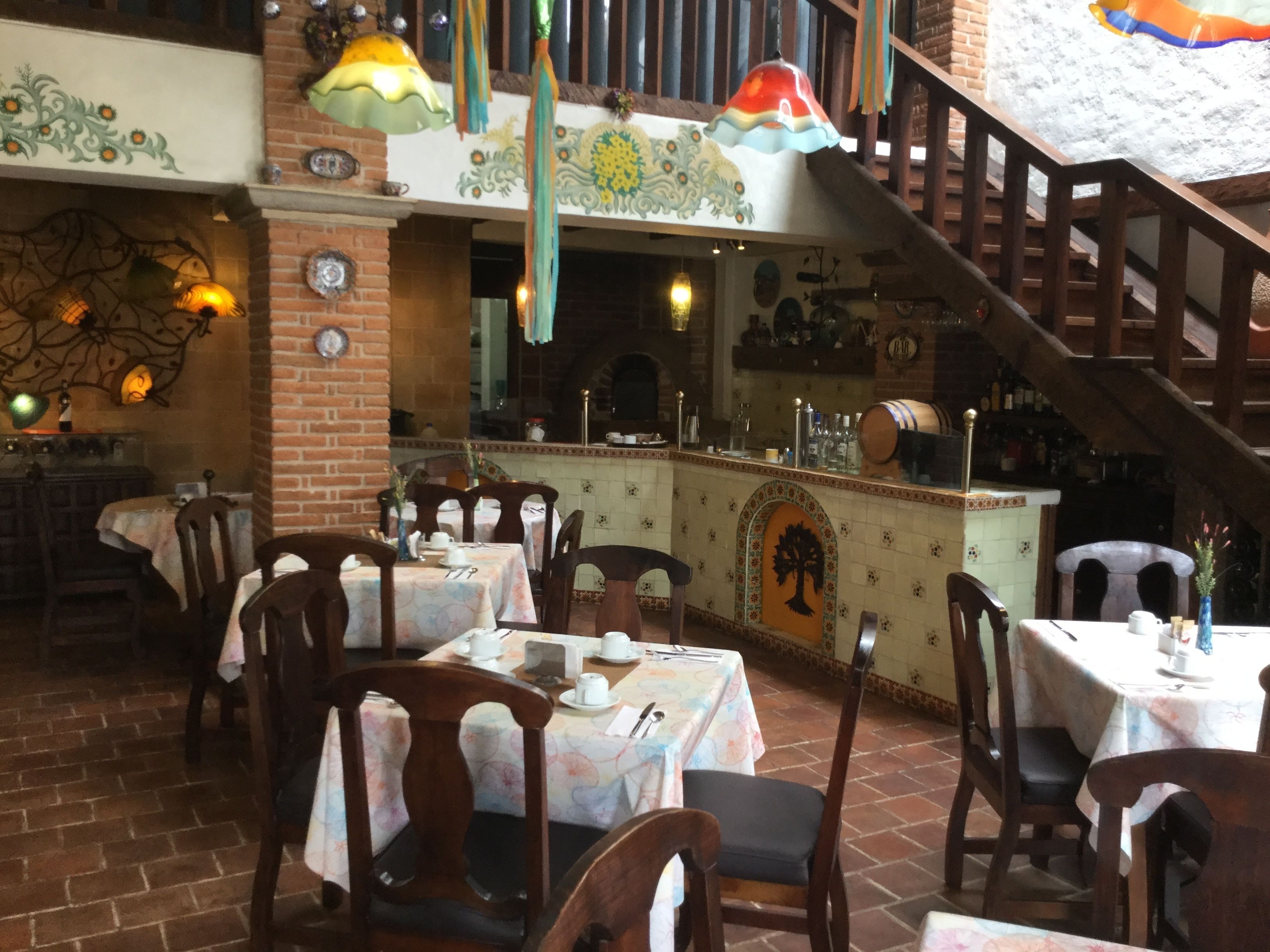 Restaurante com paredes de tijolo, mesas de madeira e luminárias pendentes.