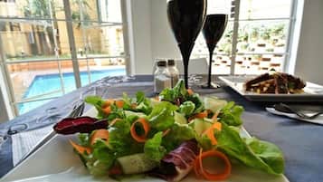 Uma mesa de jantar com uma salada, dois copos de vinho e um prato de comida.