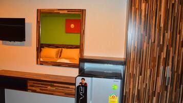 Quarto de hotel com cama, televisão fixada na parede e painel de parede de madeira.
