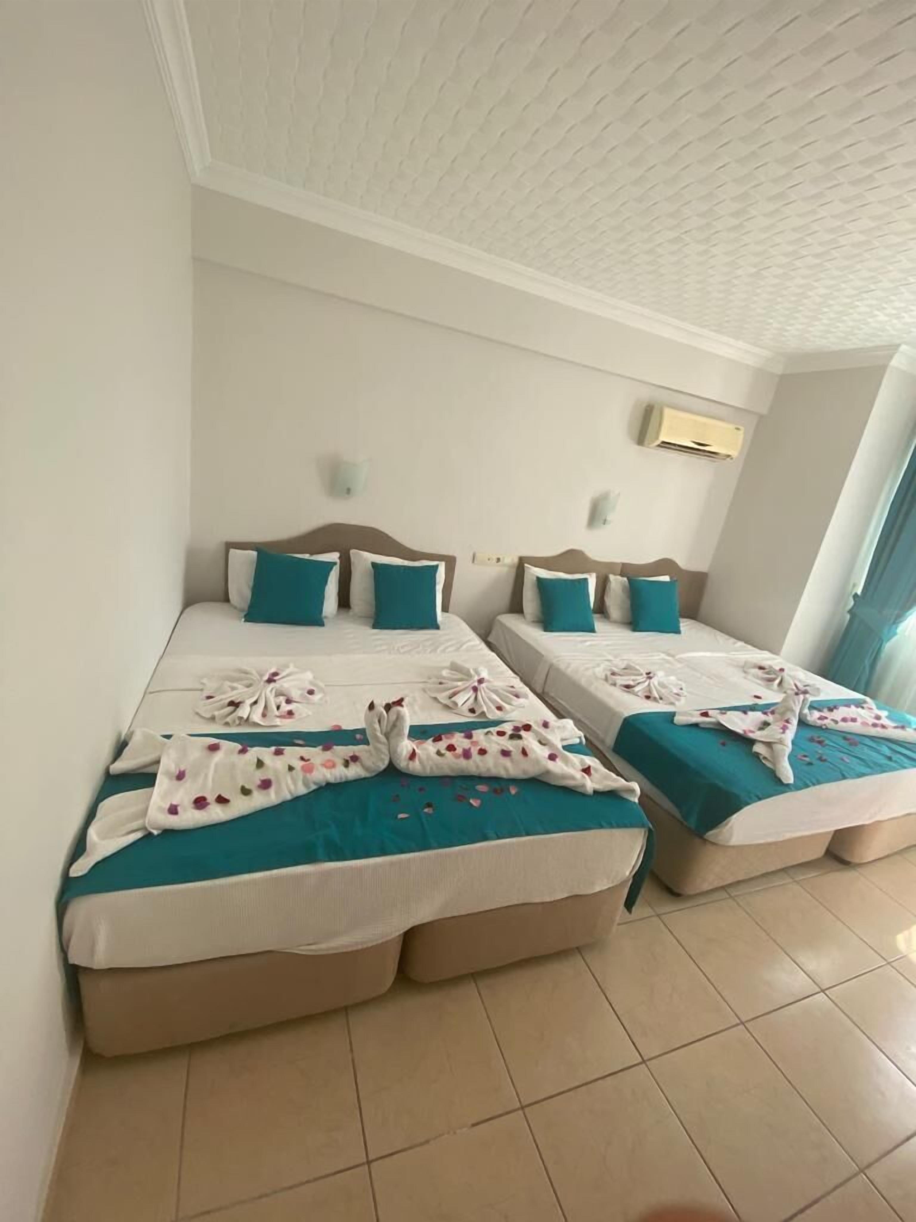 Quarto de hotel com duas camas, cada uma com roupa de cama azul-turquesa e branca, e teto com padrão texturizado.