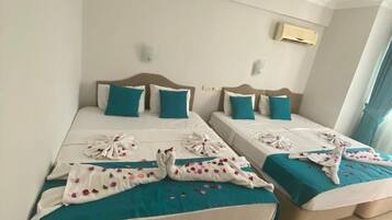 Quarto de hotel com duas camas, cada uma com roupa de cama azul-turquesa e branca, e teto com padrão texturizado.