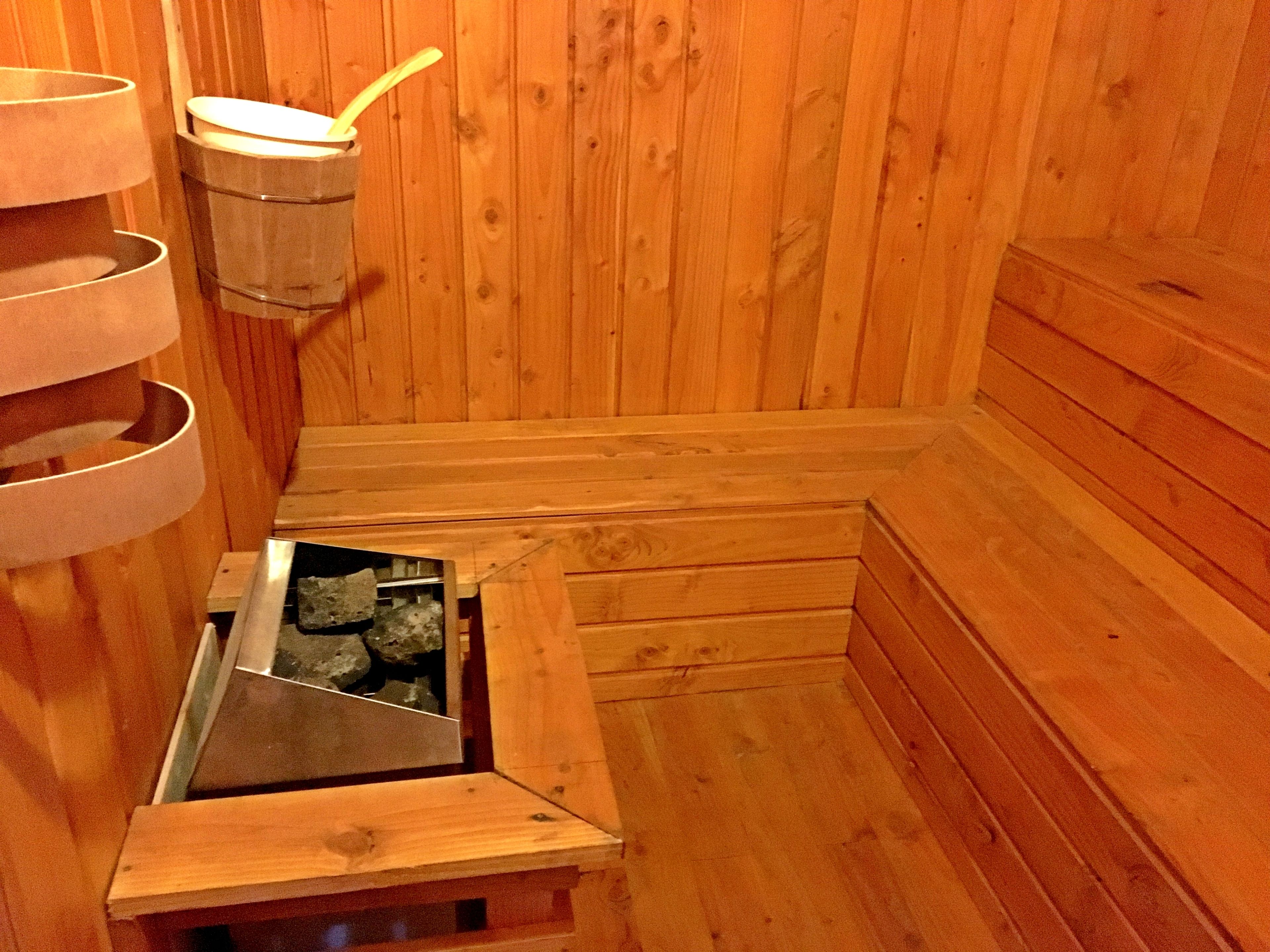 Uma sauna de madeira com um banco, uma pia com maçaneta amarela e um recipiente de metal com pedras.