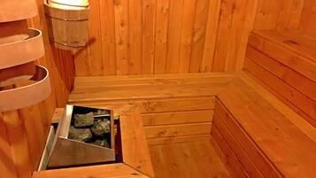 Uma sauna de madeira com um banco, uma pia com maçaneta amarela e um recipiente de metal com pedras.