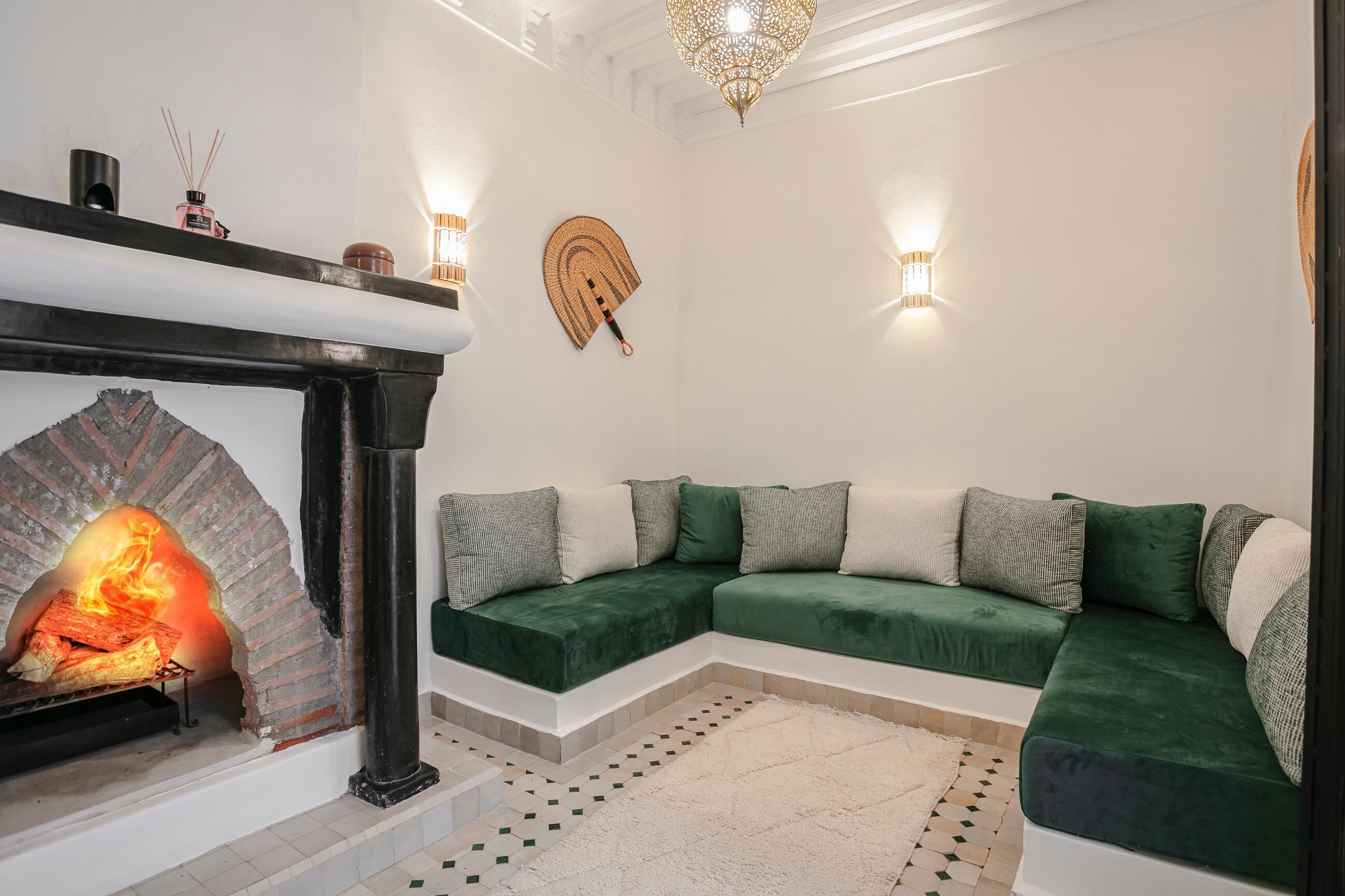 Uma sala de estar acolhedora com lareira, sofá seccional verde, tapete estampado e arandelas decorativas.