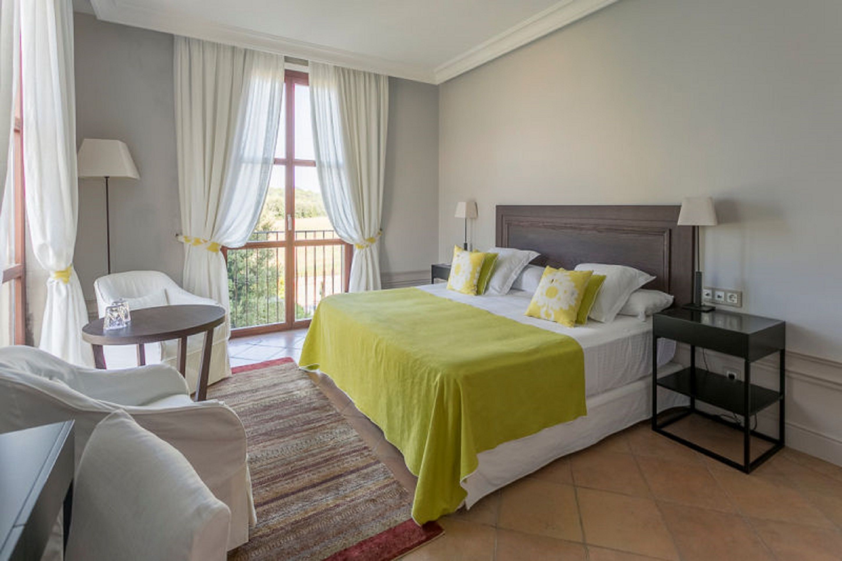Quarto com cama, mesas de cabeceira, uma cadeira e vista para o exterior.