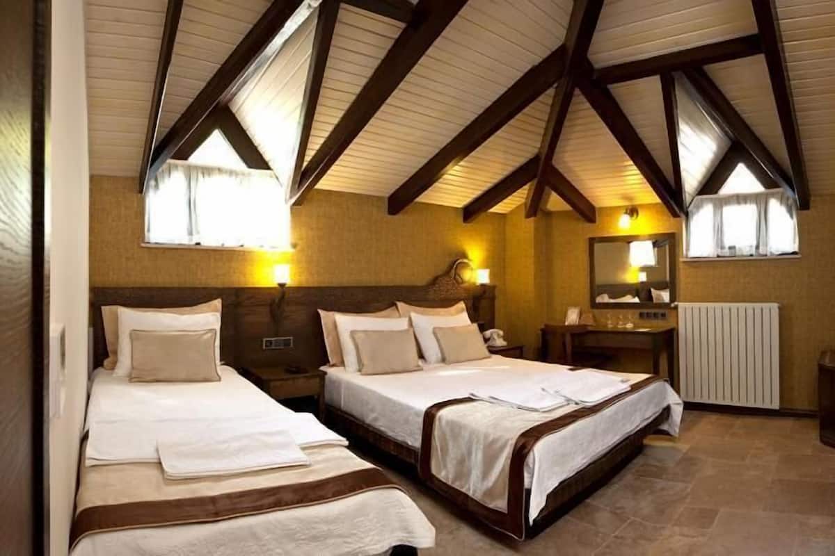 Quarto de hotel com duas camas, teto de madeira, uma pequena escrivaninha e um espelho.