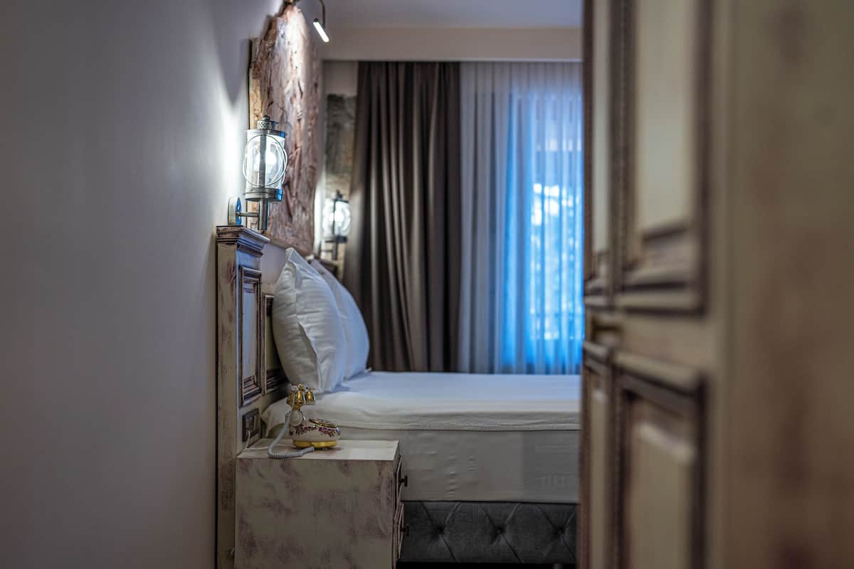 Quarto com cama, mesa de cabeceira, luminária e cortinas.