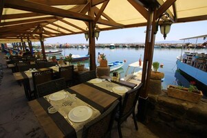 Restaurante à beira-mar com mesas preparadas para refeições, com vista para uma marina e barcos.
