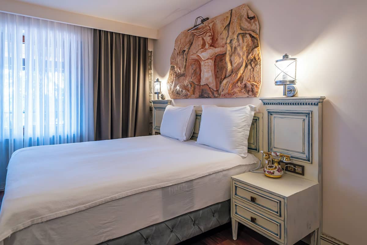 Quarto de hotel com uma cama grande, uma mesa de cabeceira com abajur e um quadro grande na parede.