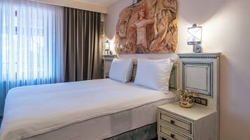 Quarto de hotel com uma cama grande, uma mesa de cabeceira com abajur e um quadro grande na parede.