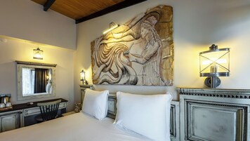 Quarto de hotel com uma cama grande, uma lareira clássica, um quadro abstrato e um candelabro.