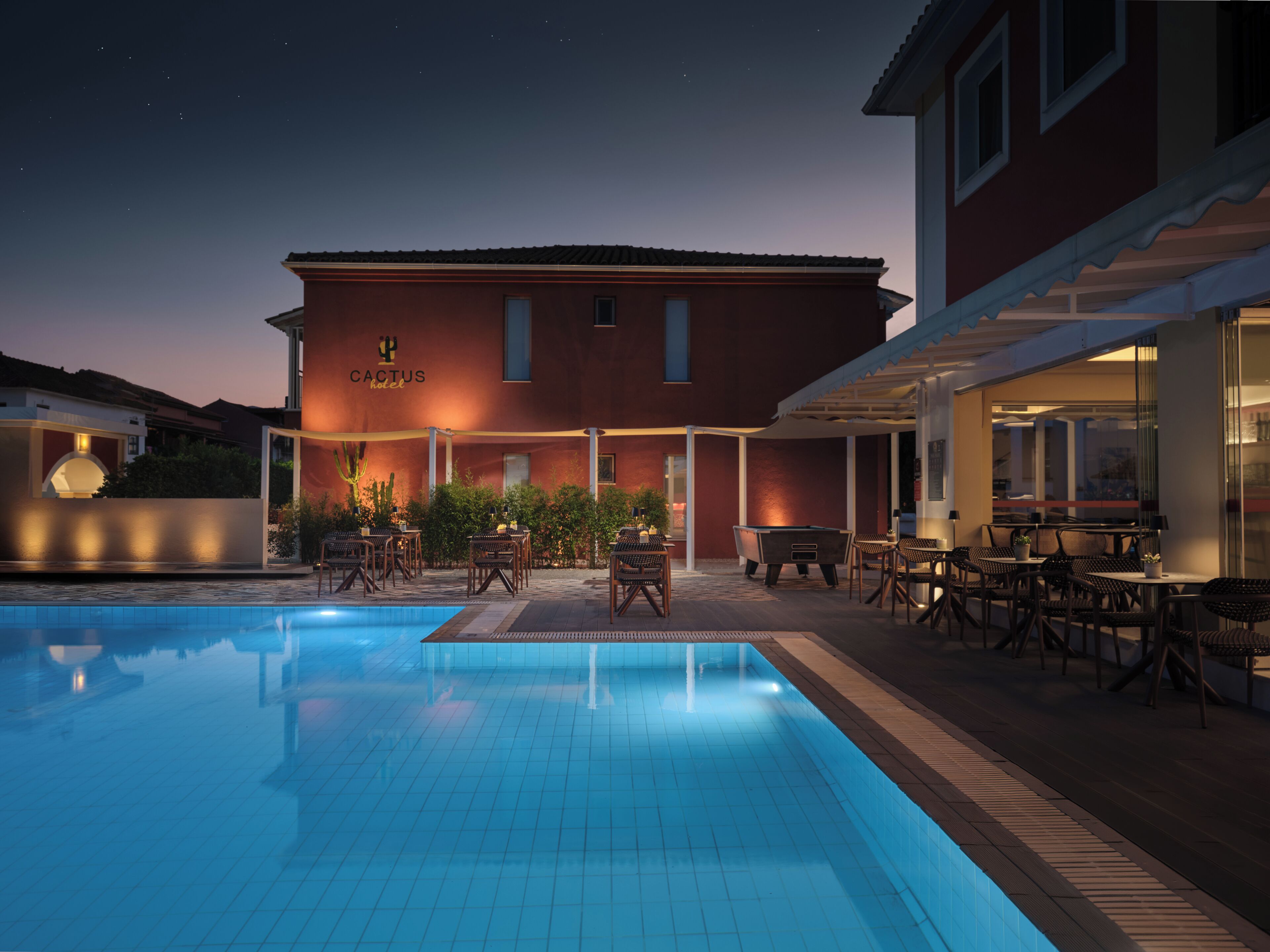 Um hotel chamado 'Cactus' com piscina, área de estar externa e fachada vermelha.