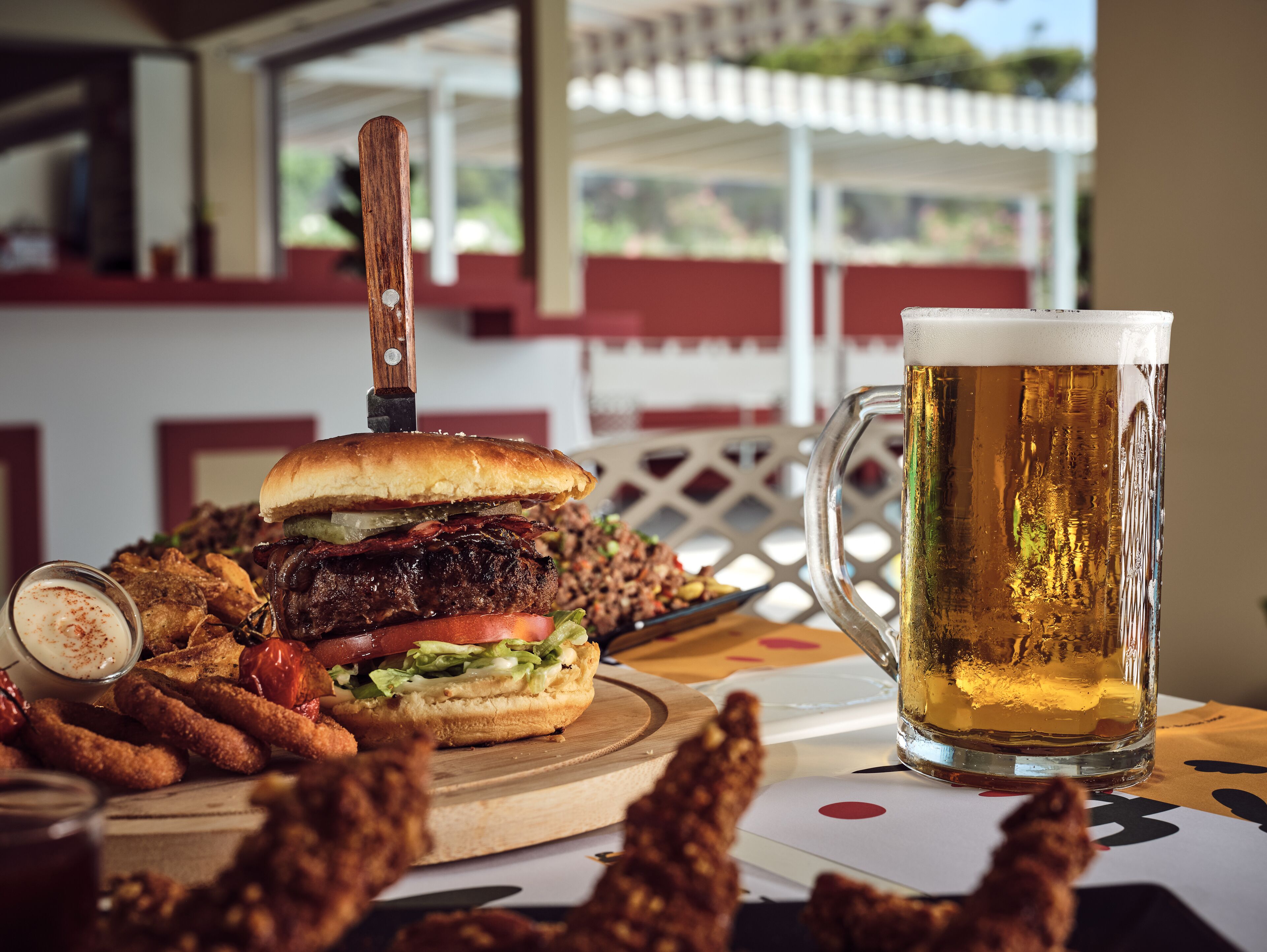 Uma refeição com um hambúrguer, batatas fritas e uma caneca de cerveja sobre uma mesa.