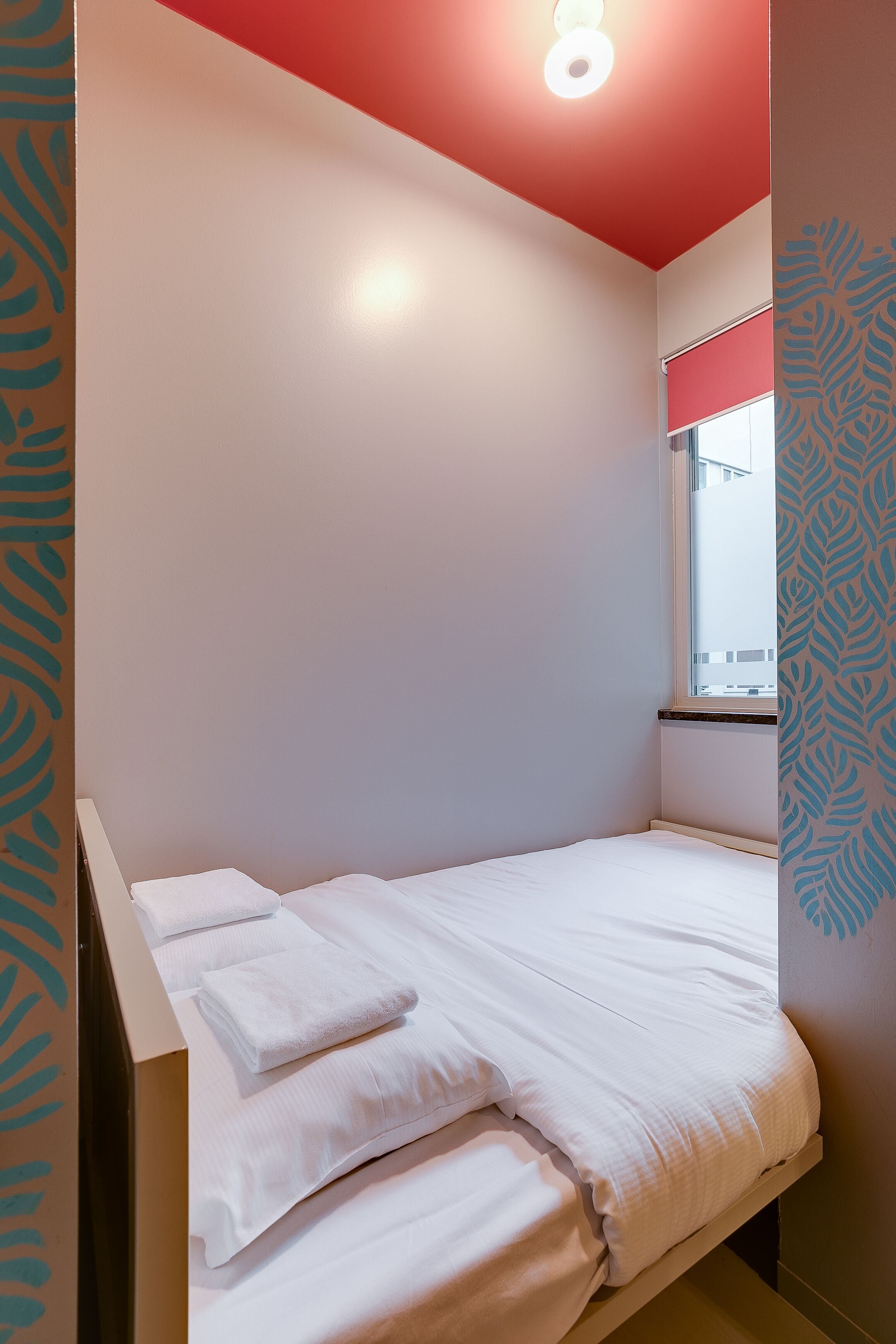 Uma cama de solteiro com roupa de cama branca num quarto com teto vermelho e janela com vista para o exterior.
