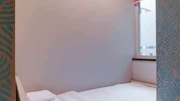 Uma cama de solteiro com roupa de cama branca num quarto com teto vermelho e janela com vista para o exterior.