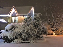 Paisagem coberta de neve com uma casa de fachada em pedra e telhado inclinado.