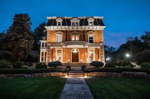 Uma casa grande de dois andares, construída em tijolo, com fachada simétrica, entrada central e um gramado bem cuidado.